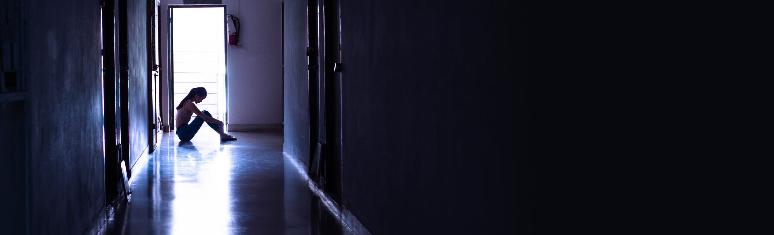 Silhouette of a sad young girl sitting in the dark, thinking abo ...